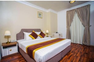 Quarto de hotel com uma cama grande, duas mesas de cabeceira com luminárias, um criado-mudo e uma janela com cortinas.