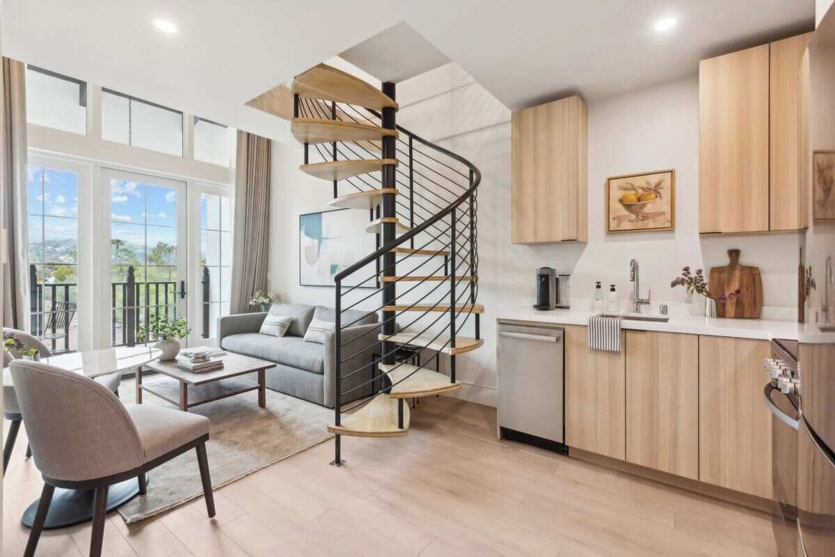 Um espaço de estar moderno com escada em espiral, cozinha com armários de madeira e vista para o exterior.