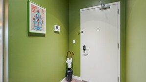 Um corredor com parede verde, porta branca, quadro emoldurado e um objeto preto com um item branco em cima.