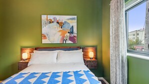 Quarto de hotel com uma cama, duas luminárias de cabeceira, um quadro na parede e uma janela com cortinas.