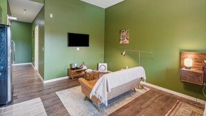 Uma sala de estar moderna com parede verde, uma TV de tela plana, um sofá, uma mesa de centro e um armário de madeira com uma luminária.