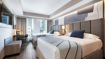 Quarto de hotel moderno com duas camas, uma mesa de trabalho e uma grande janela com vista para a cidade.