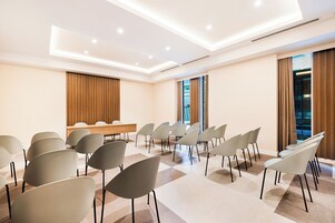 Uma sala de conferências com uma mesa comprida e várias cadeiras, janelas amplas com cortinas e um design moderno no teto.
