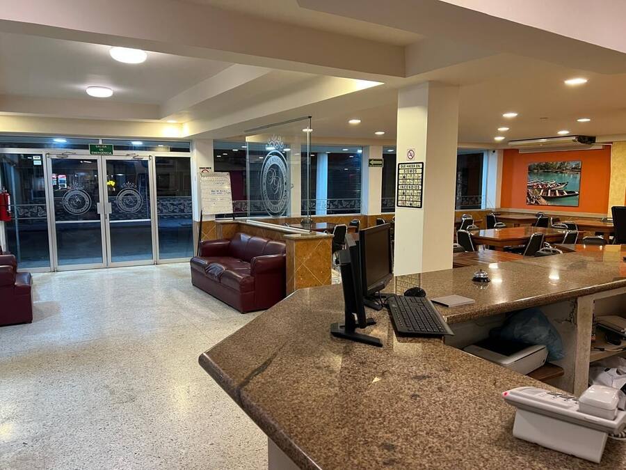 Um saguão de hotel com balcão de recepção, área de estar e entrada por porta de vidro.