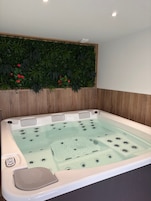Uma banheira de hidromassagem com vários jatos, painel de controle e parede de madeira com folhagem verde e flores vermelhas.