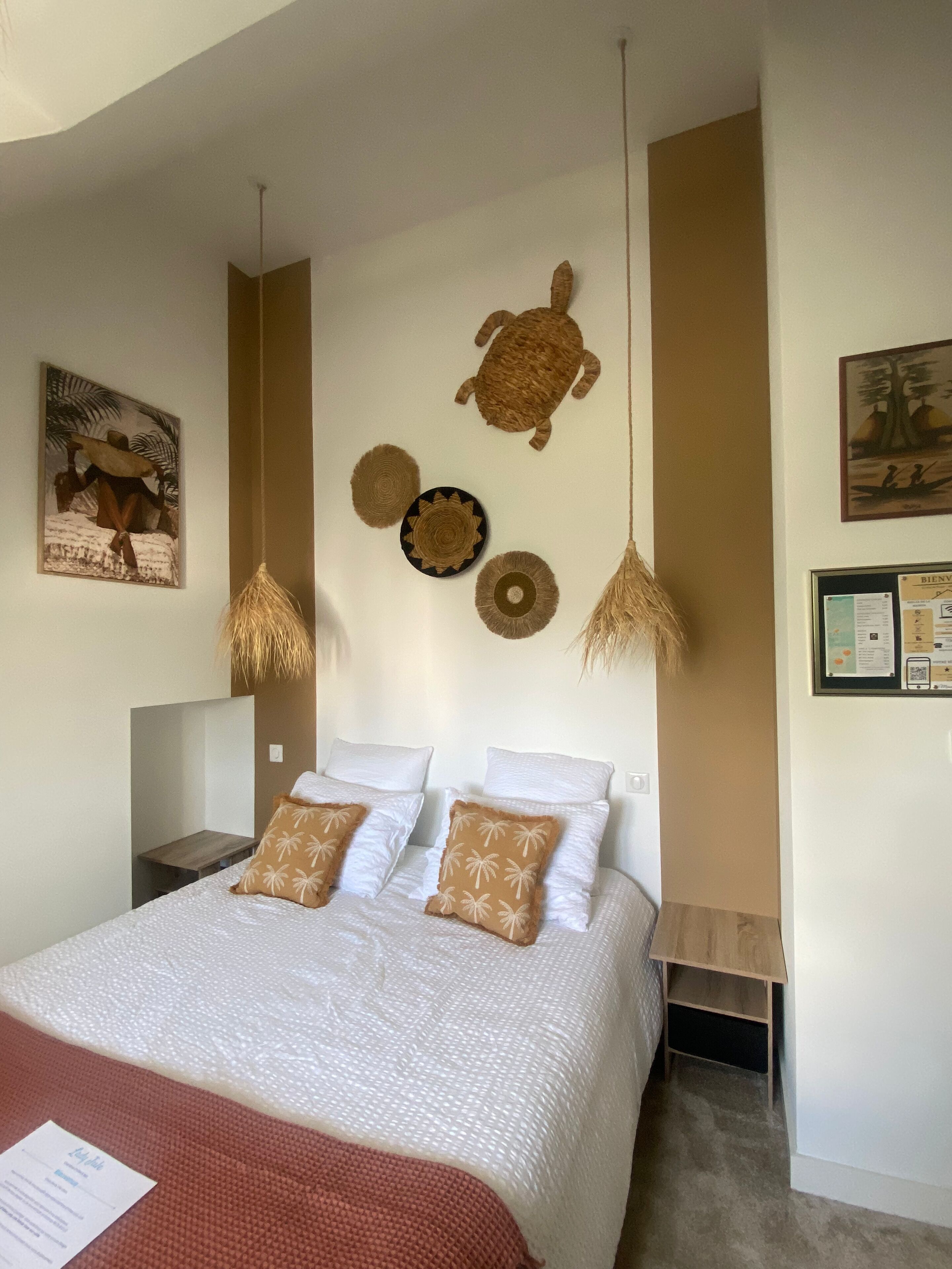 Quarto com uma cama grande, duas mesas de cabeceira, um espelho e detalhes na parede, incluindo uma tartaruga e padrões circulares.