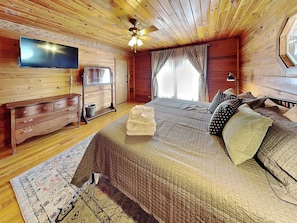 Quarto de cabana de madeira com cama, cômoda, televisão e ventilador de teto.