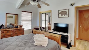 Quarto com uma cama grande, ventoinha no teto, televisão, cômoda e uma porta.