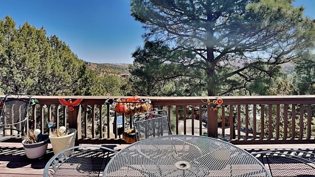 Um terraço com mesa e cadeiras de metal, rodeado por plantas em vasos e uma grande árvore.