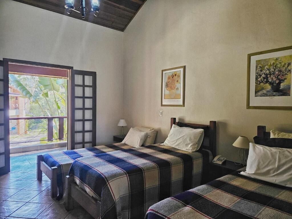Quarto de hotel com duas camas, uma mesinha e varanda com vista para áreas verdes.
