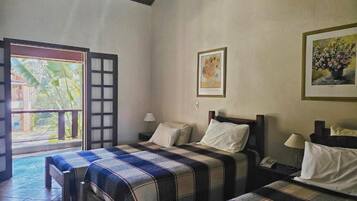 Quarto de hotel com duas camas, uma mesinha e varanda com vista para áreas verdes.
