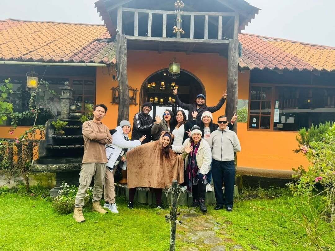 Um grupo de pessoas posando em frente a um edifício com telhado de azulejos e uma fonte de pedra.
