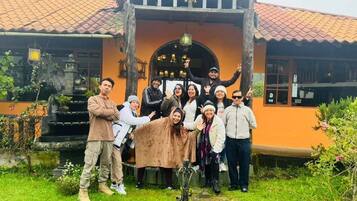 Um grupo de pessoas posando em frente a um edifício com telhado de azulejos e uma fonte de pedra.