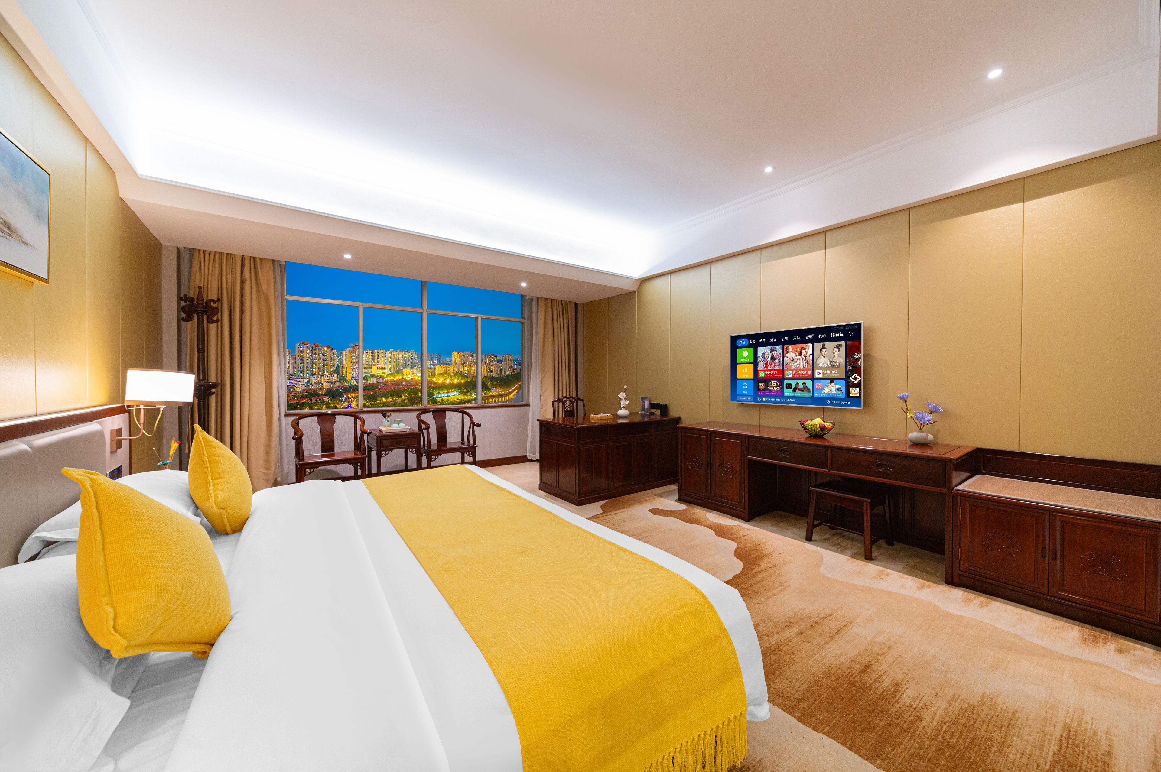 Quarto de hotel com uma cama grande, uma escrivaninha, uma cadeira, uma televisão e vista para a cidade.