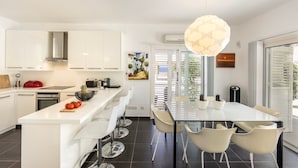 Cozinha moderna com armários brancos, uma ilha central com banquetas, uma mesa de jantar com cadeiras e uma luminária pendente.