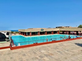 Piscina com vista para o oceano, área de estar coberta e um edifício com uma placa.