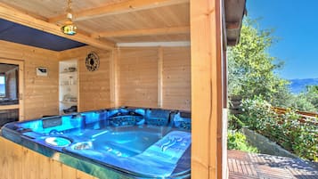 Uma área de spa em madeira com hidromassagem, paredes de madeira e vista para vegetação e montanhas.