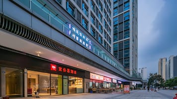 Hotel moderno com fachada de vidro, área de estar ao ar livre e sinalização das comodidades.