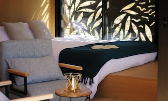 Um quarto aconchegante com uma cama, uma cadeira e uma mesinha com abajur.