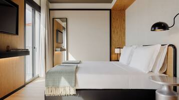 Quarto de hotel moderno com uma cama grande, mesa de cabeceira, televisão de tela plana na parede e uma janela ampla com cortinas.