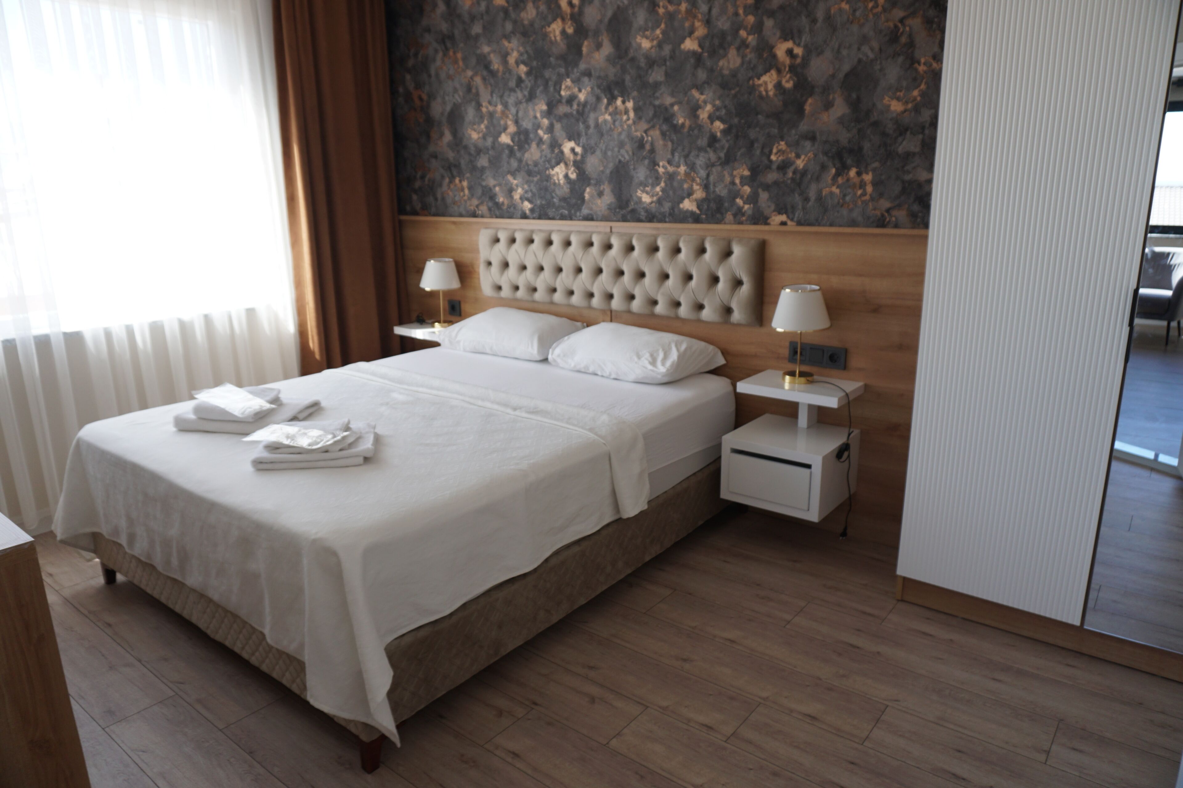 Cama bem arrumada com lençóis e toalhas brancos, cabeceira de madeira e mesa de cabeceira com abajur.