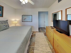 Quarto com cama, televisão em uma cômoda, quadro na parede e porta para outro aposento.