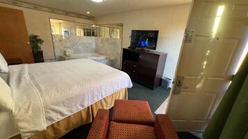 Quarto de hotel com uma cama grande, televisão, cômoda e porta.