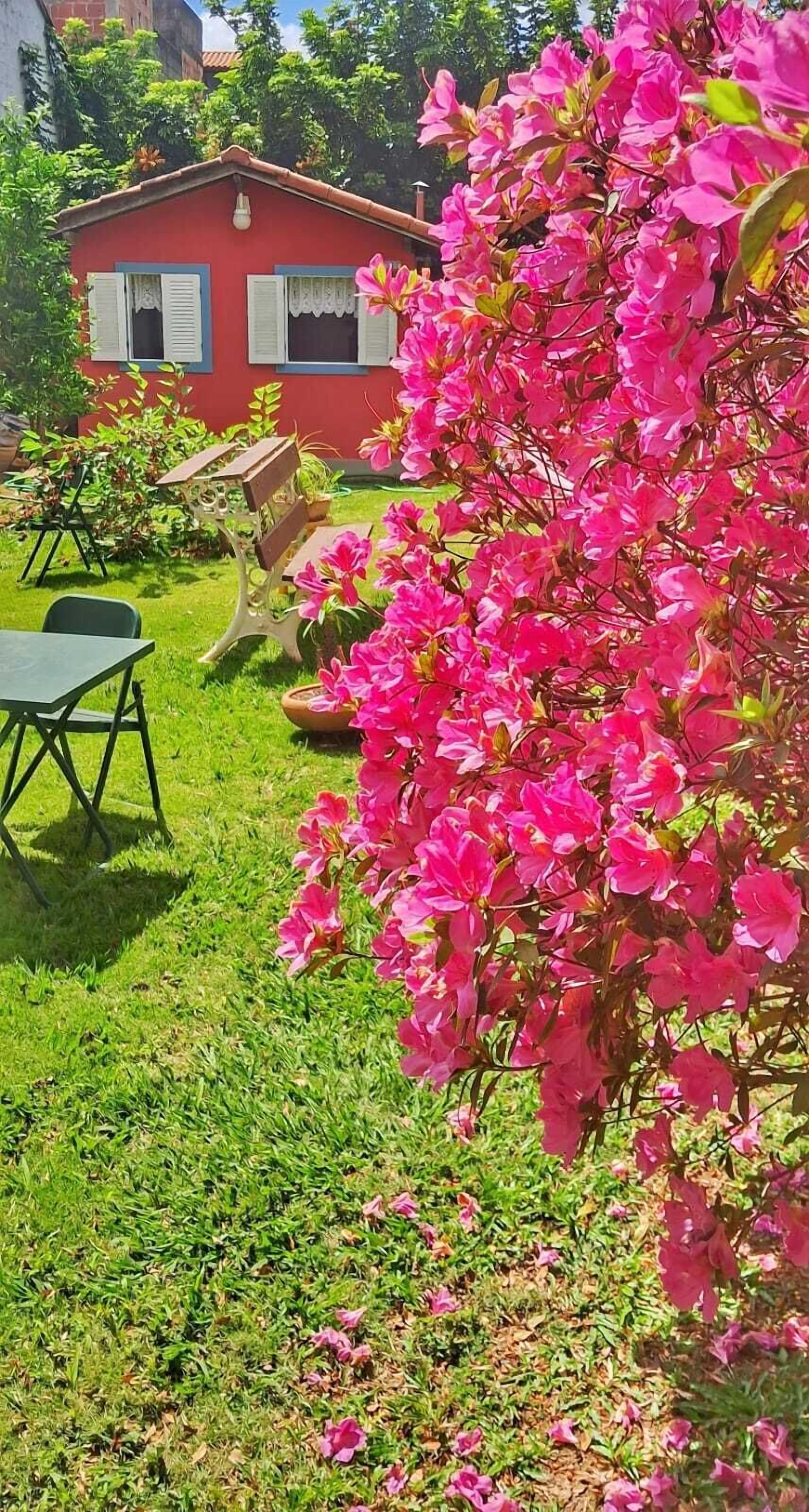Um edifício vermelho com janelas em branco, gramado verde e flores cor-de-rosa.