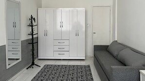 Quarto com um guarda-roupa branco grande, um sofá cinza e um tapete preto e branco.