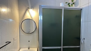 Casa de banho com lavatório branco, espelho redondo e cabine de duche em vidro.