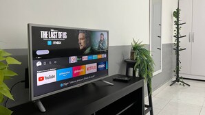 Televisão de tela plana em suporte preto exibindo um filme com diversos ícones de serviços de streaming abaixo.