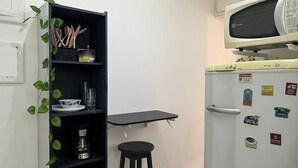Cozinha com frigorífico, micro-ondas e um armário preto com utensílios de cozinha.