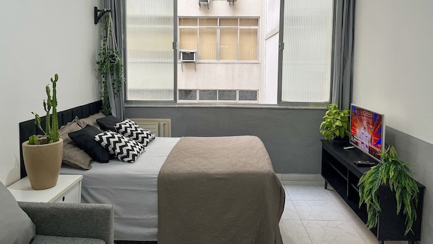 Quarto com cama, janela com cortinas, televisão e um vaso com planta.