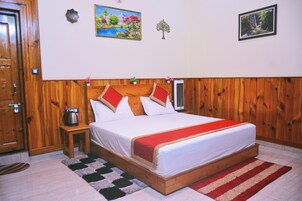 Uma cama bem arrumada com cabeceira de madeira, uma pequena mesa de cabeceira com uma chaleira e um cobertor vermelho.