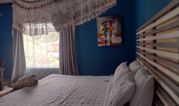 Quarto com cama, cortinas, janela e um quadro na parede.