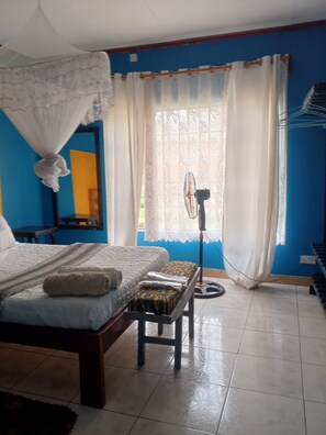 Quarto com cama, mesa de cabeceira e ventilador.