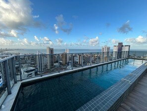 Piscina infinita no terraço, com vista para o horizonte urbano, incluindo edif ícios altos e uma costa distante.
