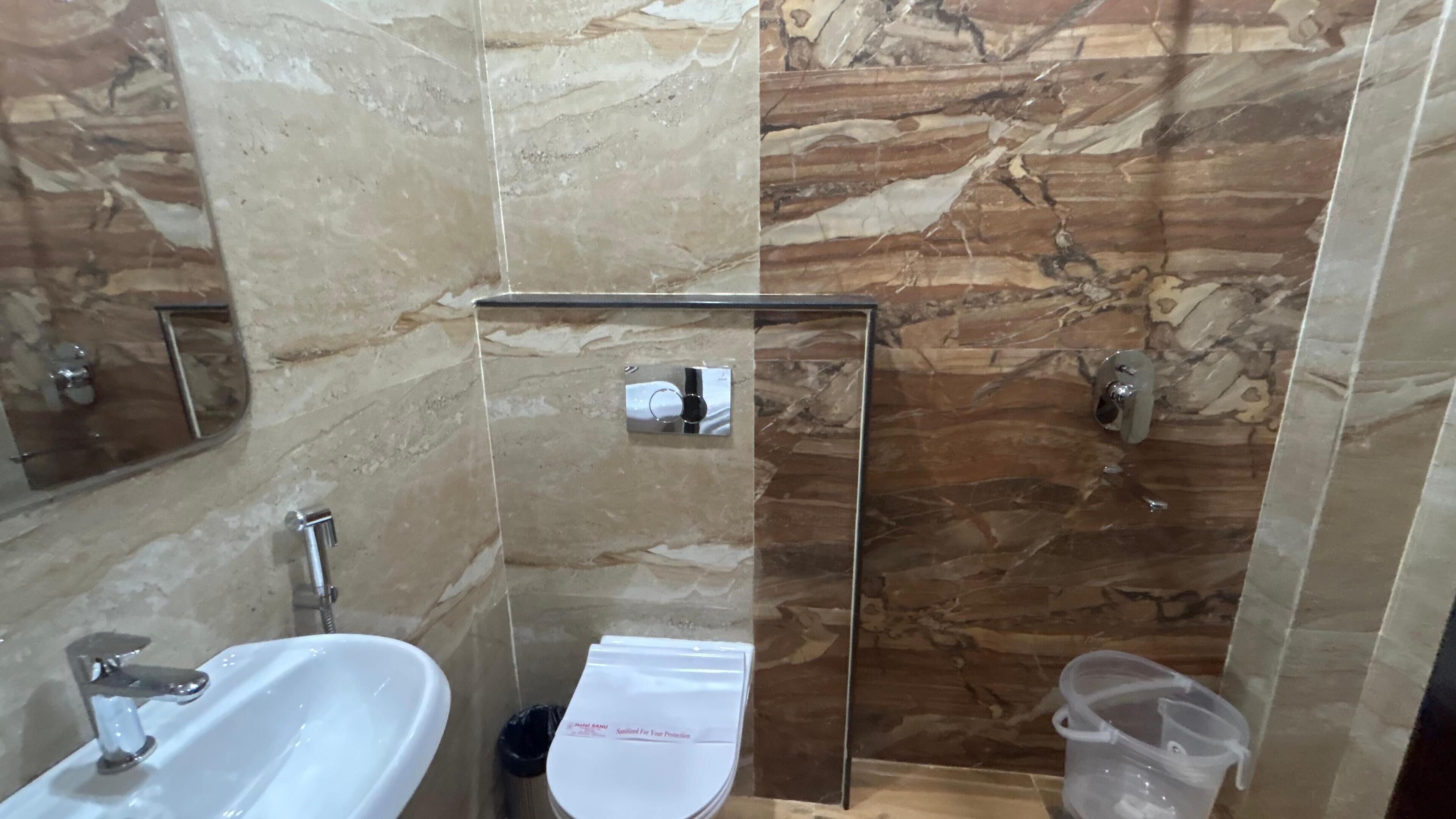 Um banheiro com parede de mármore, box de vidro, pia e vaso sanitário.