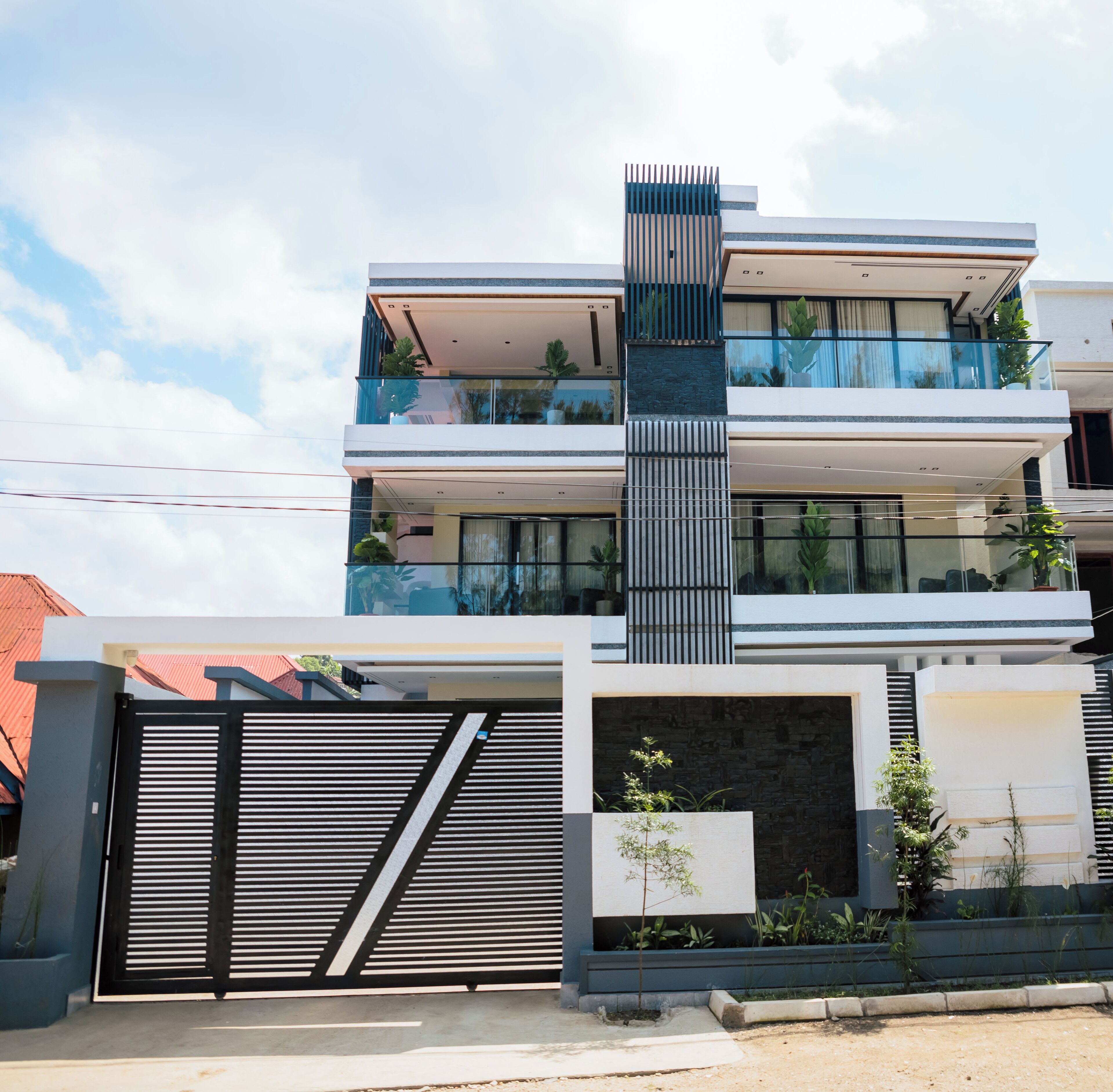 Uma casa moderna de dois andares com portão fechado, grandes janelas e uma varanda.