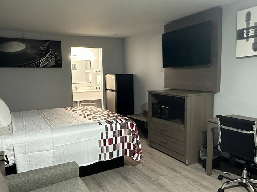 Quarto com cama, escrivaninha, cadeira, televisão e porta.