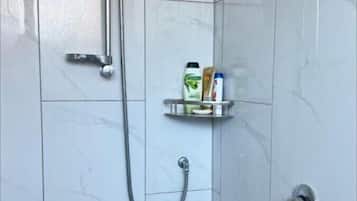 Chuveiro com chuveiro manual e torneira fixada na parede. Há uma prateleira com artigos de higiene pessoal.