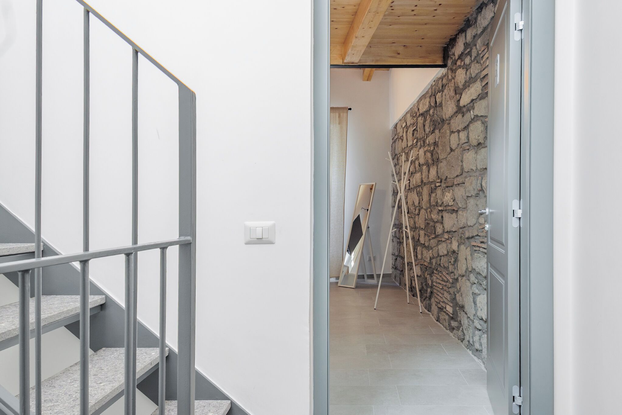 Uma escadaria com corrimãos de metal leva a um quarto com parede de pedra e uma porta.