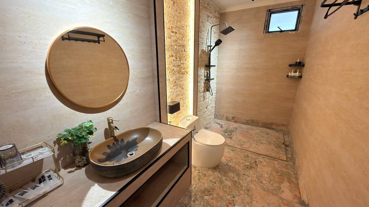 Casa de banho moderna com espelho redondo, lavatório suspenso, sanita e área de duche.