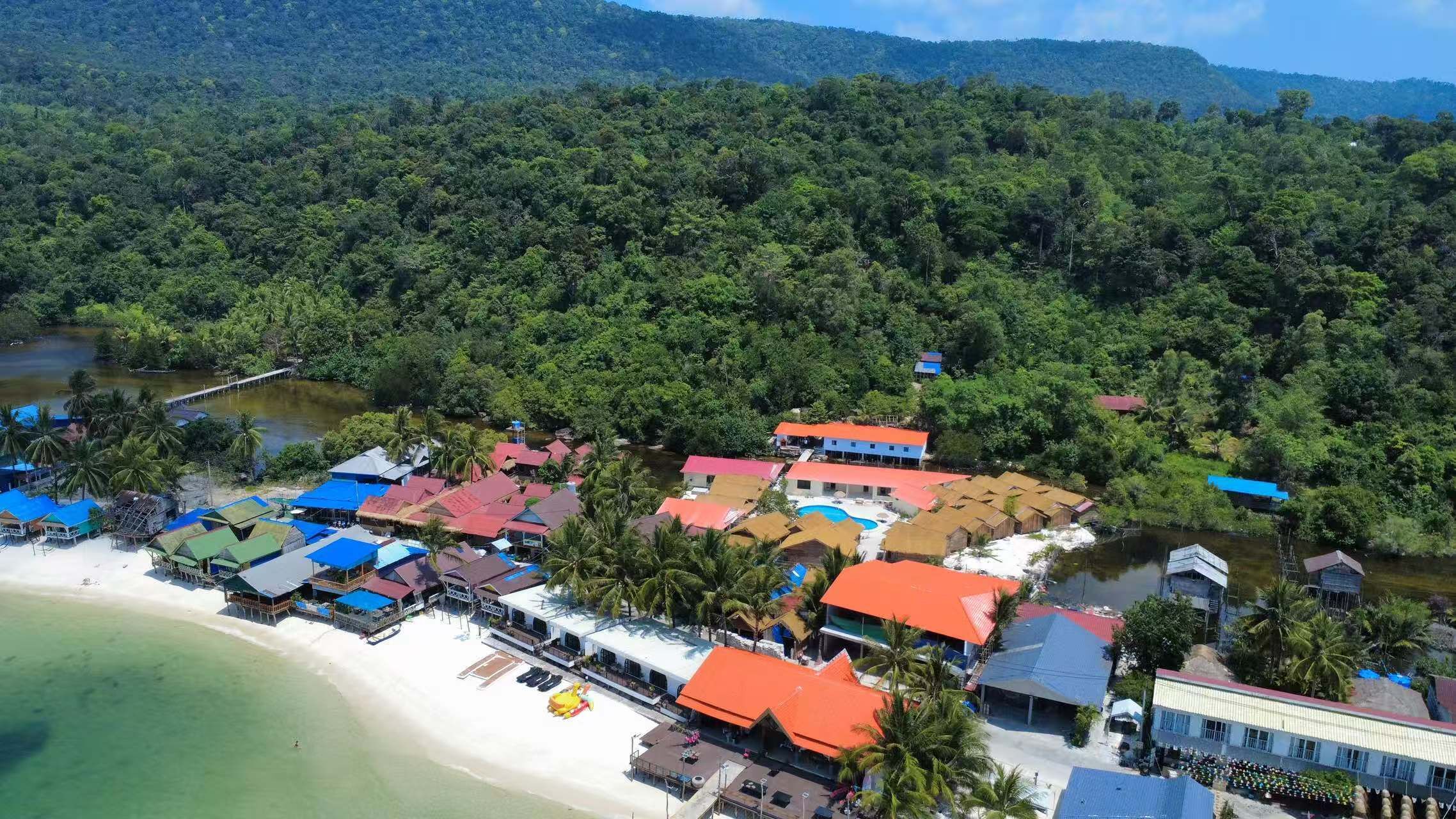 Um resort à beira-mar com cabanas de praia, piscina e um cenário arborizado.