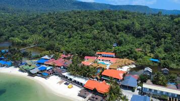 Um resort à beira-mar com cabanas de praia, piscina e um cenário arborizado.