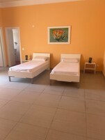 Quarto com duas camas de solteiro, uma pequena mesa de cabeceira com abajur e um quadro na parede.