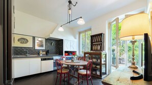 Uma cozinha com área de refeições, com uma mesa redonda, cadeiras, um lustre e vista pela janela.