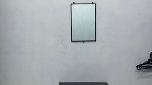 Um quarto com uma parede simples, uma pequena prateleira preta e um espelho emoldurado.