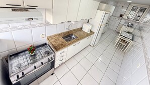 Cozinha moderna com armários brancos, bancada de granito, eletrodomésticos de aço inoxidável e piso ladrilhado.