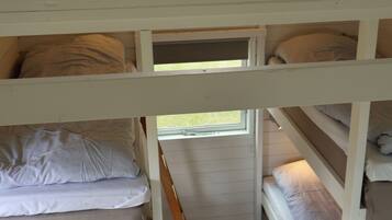 Quarto com beliche, roupa de cama branca e claraboia acima da cama de cima.